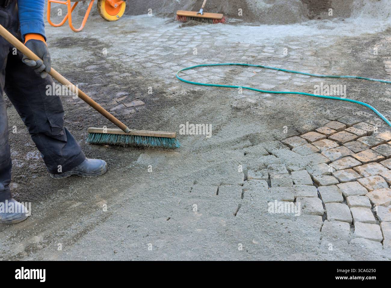 Worker cleans cobblestone street using broom tools under work day ...