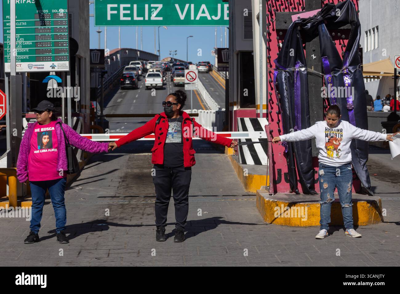 Three people reach across the Ciudad Juarez border under a "Feliz Viaje ...