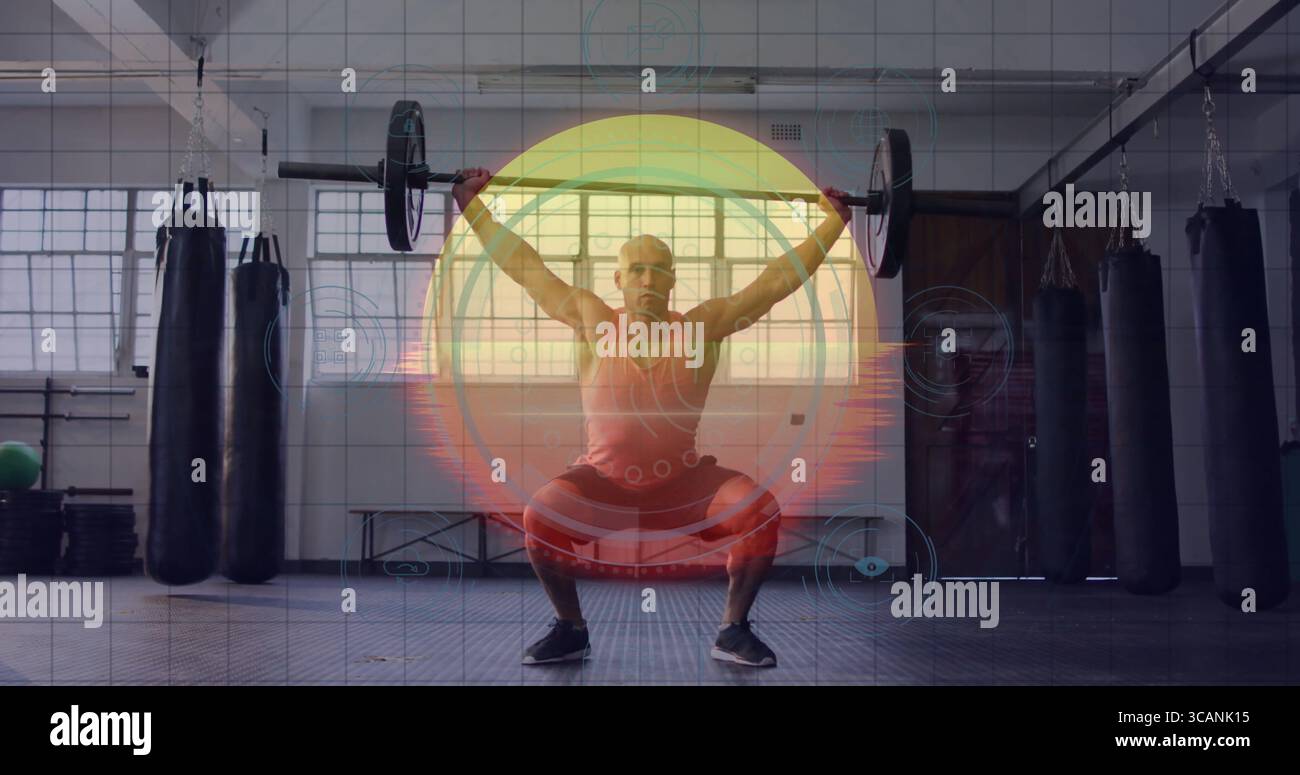 Squatting lifter in shorts holding loaded barbell overhead in gym, with ...