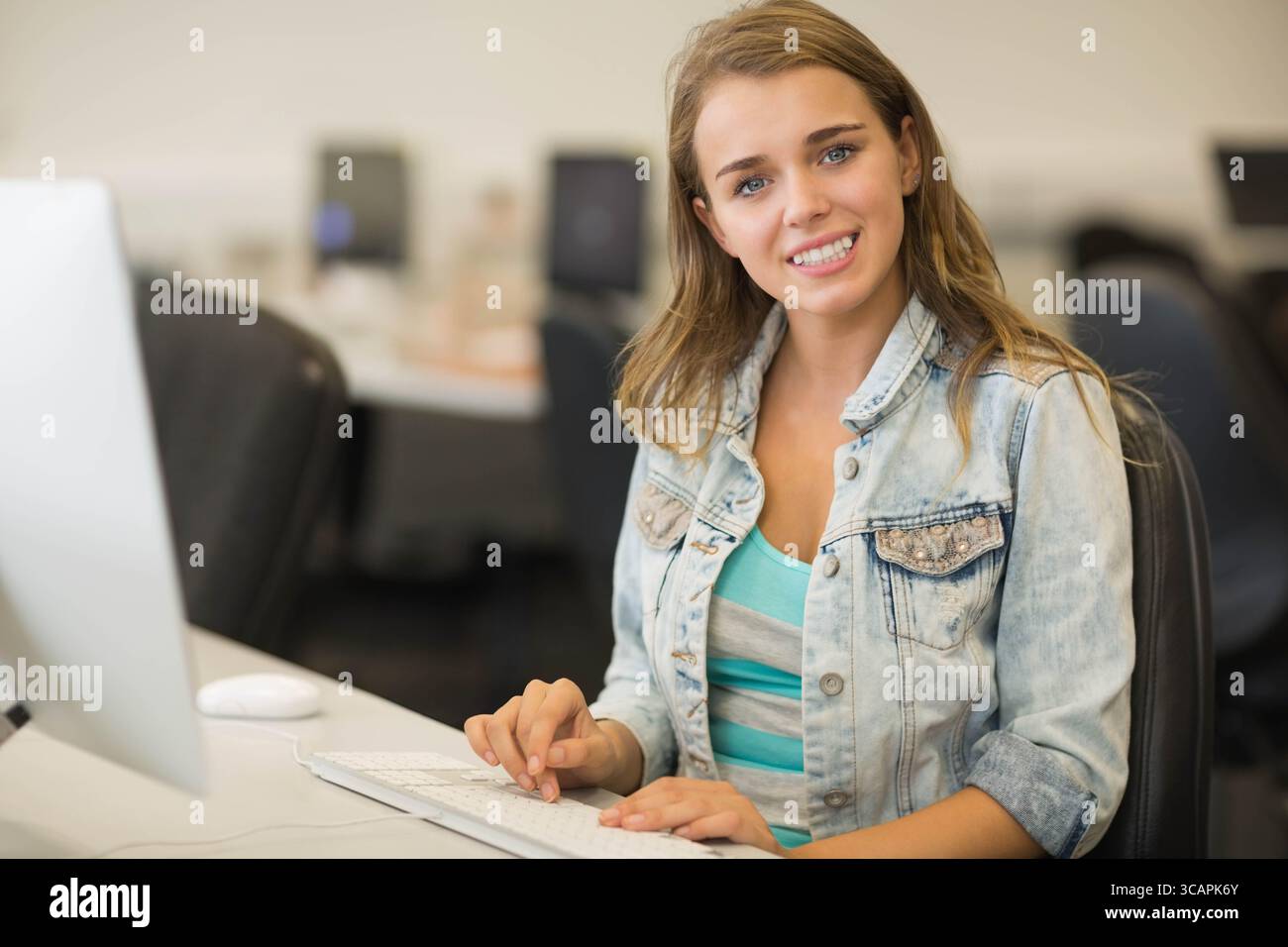 Woman typing on white keyboard at computer lab desk with desktop ...