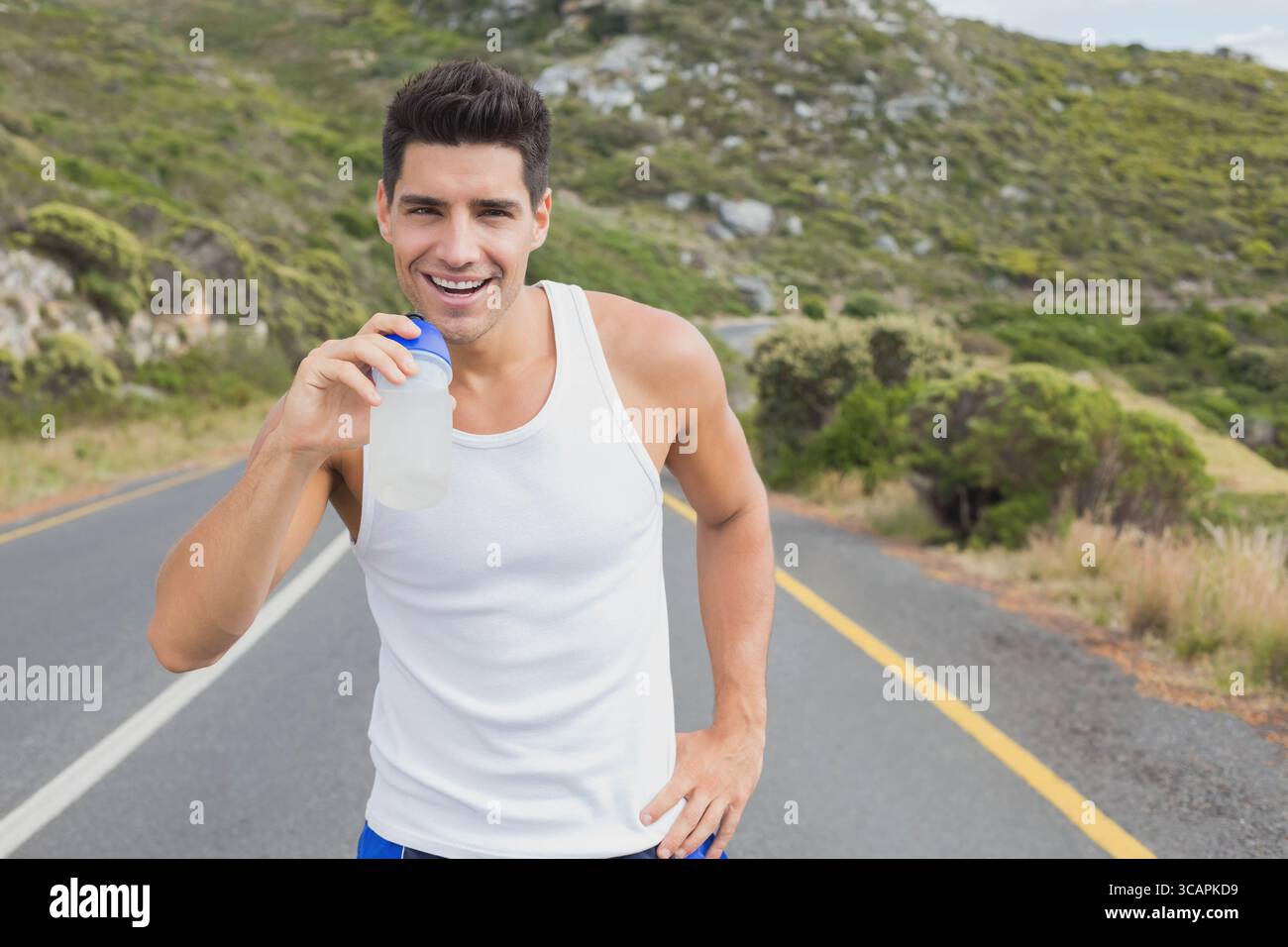 Male runner pausing on winding asphalt road through green hills ...