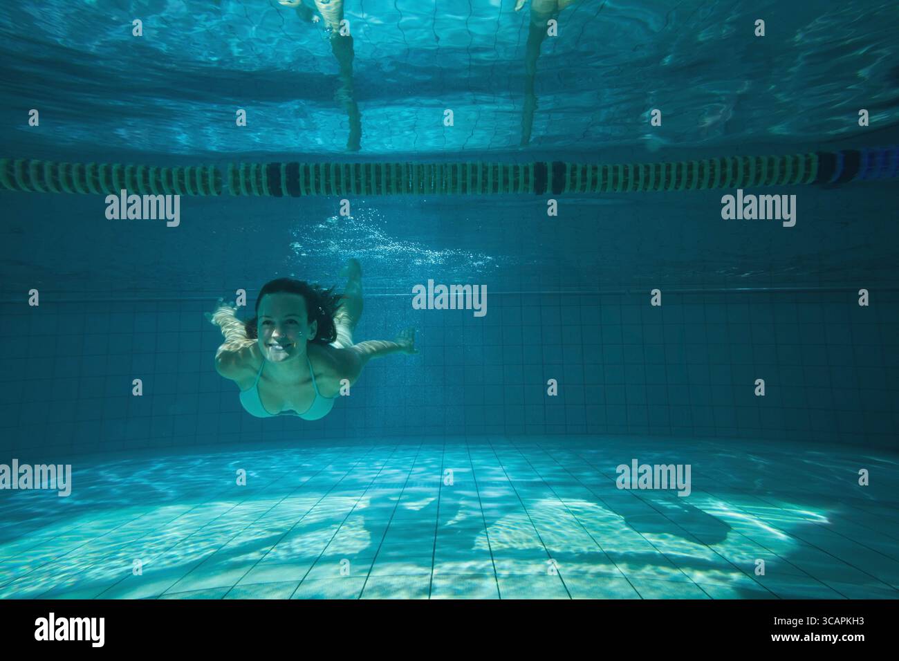Female swimmer wearing teal swimsuit gliding underwater in lane past ...
