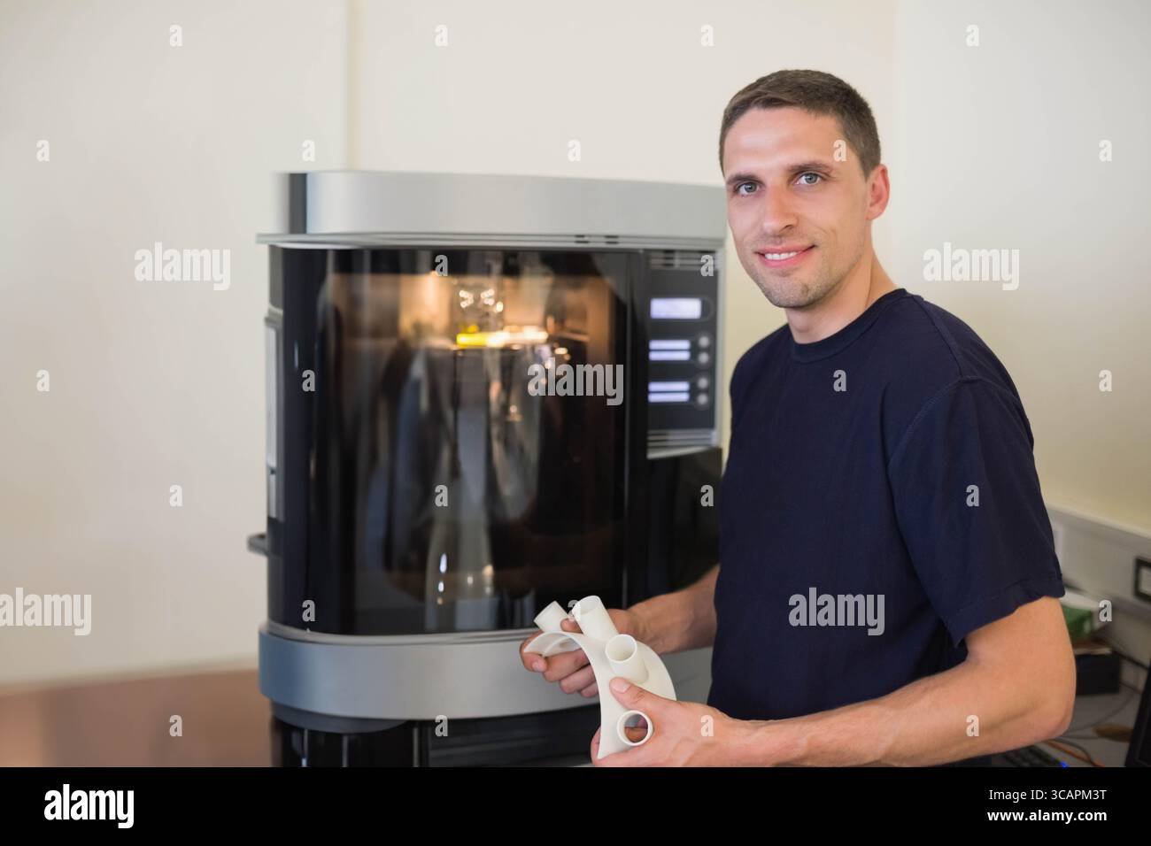 Man standing beside industrial 3D printer in workshop, holding white ...