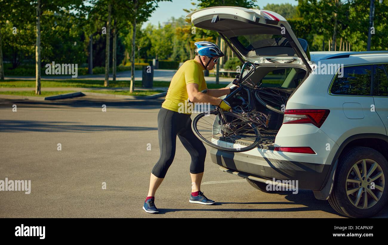 Senior man unloading road bike from car trunk in parking lot wearing ...