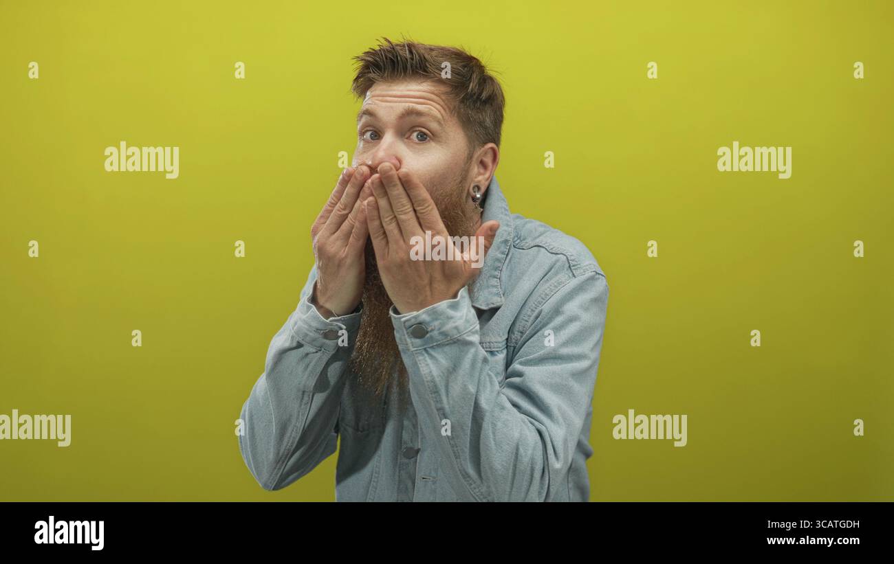 Man with ginger beard wearing denim jacket covers his mouth with both ...