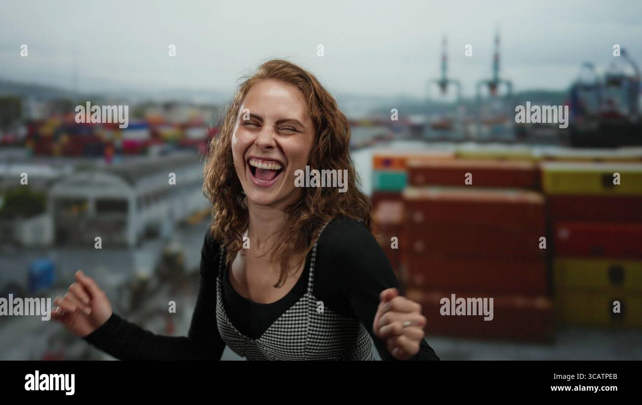 Woman laughing at seaside port with containers in background conveying ...