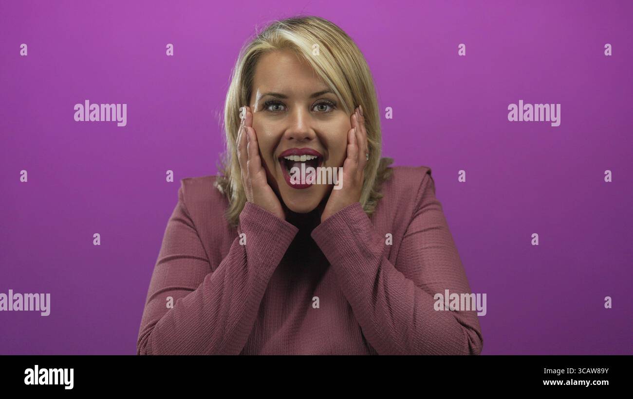 Woman holds her cheeks with both hands and opens mouth wide in studio ...