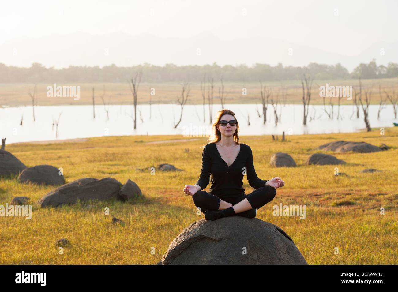 Young woman practising yoga posture by the Senanayake Samudraya Lake ...