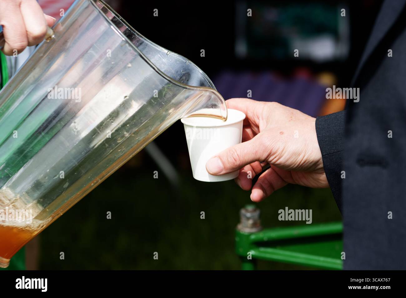 two people hands pouring cider from a plastic jug into a paper cup ...