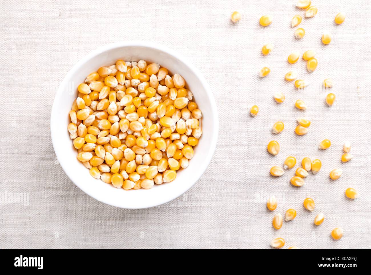 Popcorn kernels, in a white bowl on linen. Seeds of Zea mays variety ...