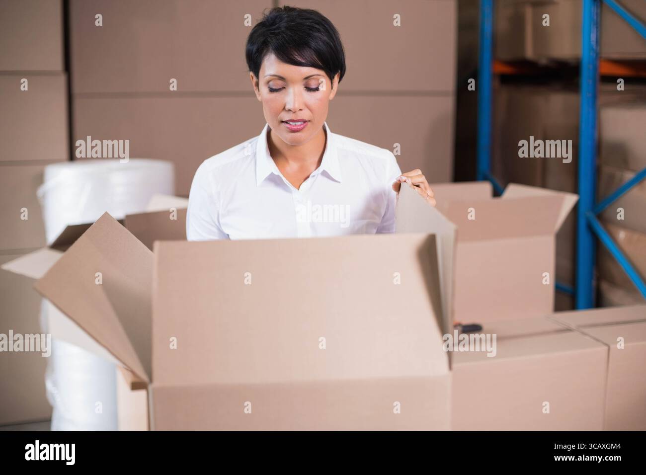 Woman in white shirt opening cardboard box in warehouse storage by ...