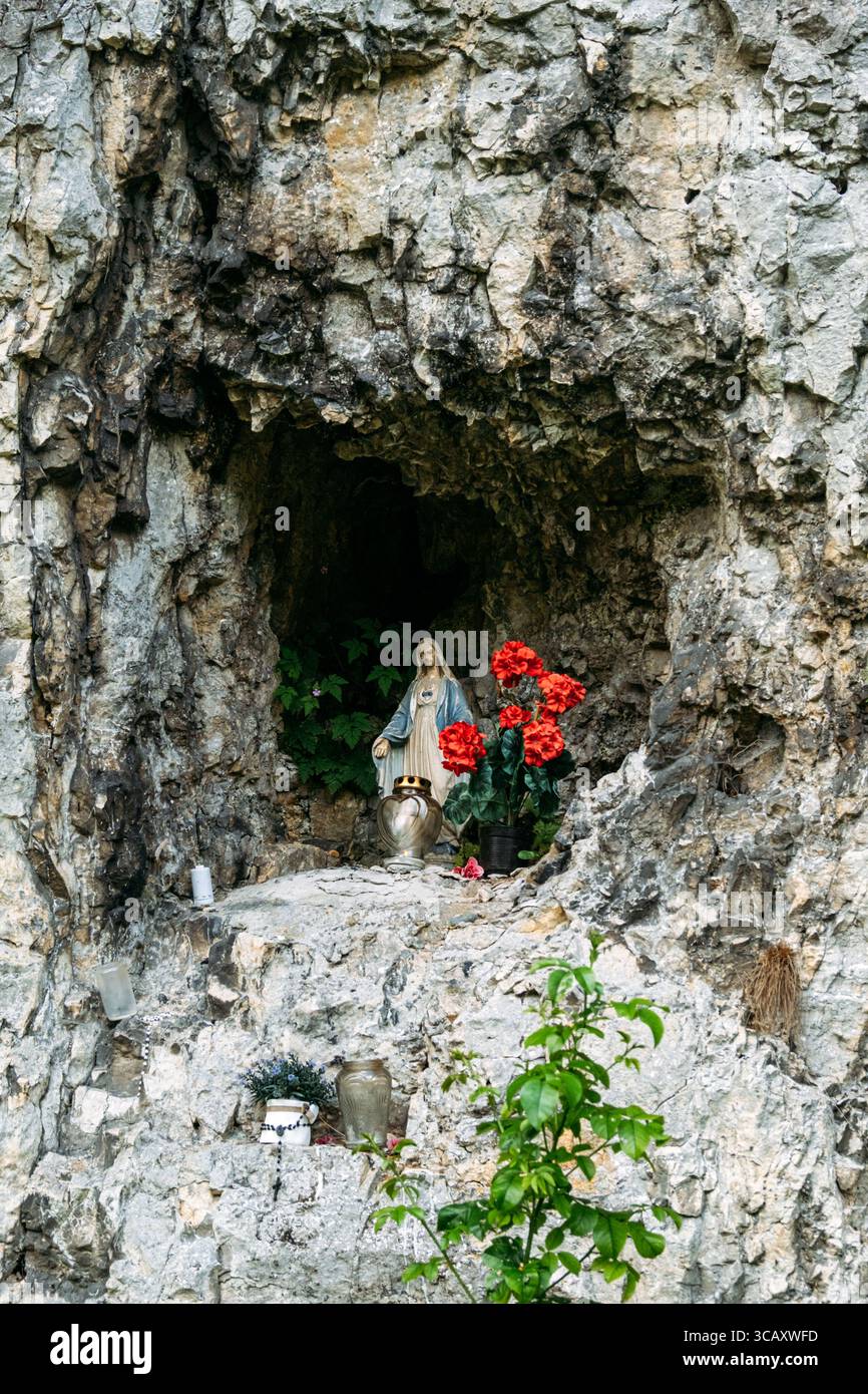 Religious shrine with a Virgin Mary statue and red flowers placed ...