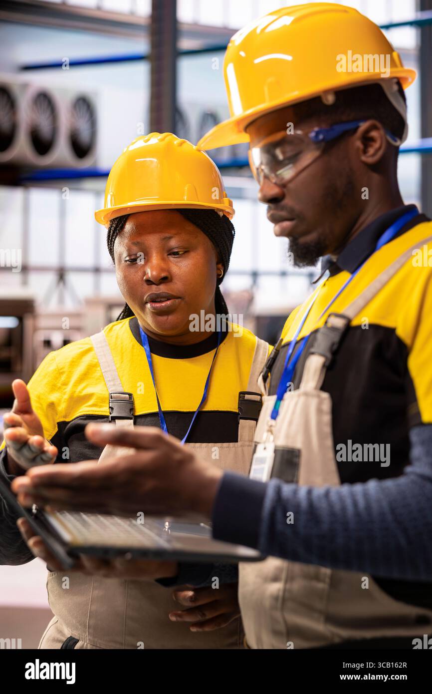 African american technicians in automated factory collaborate on optimizing a production line ...