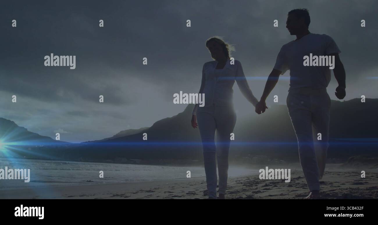 Walking mature couple holding hands along sandy shoreline at dusk, with ...