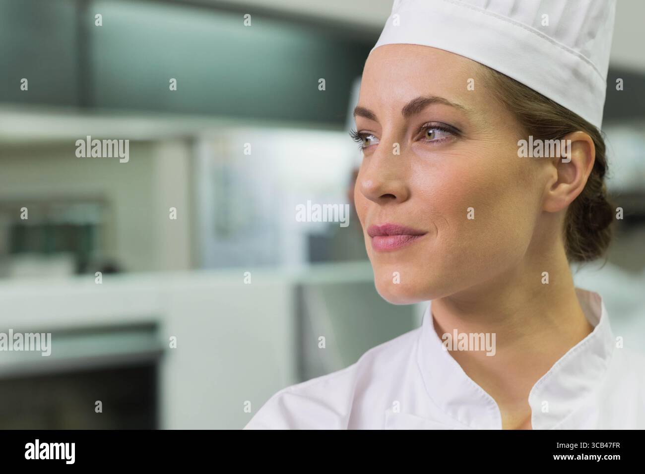 Mid adult female chef standing in kitchen by stainless counters wearing ...