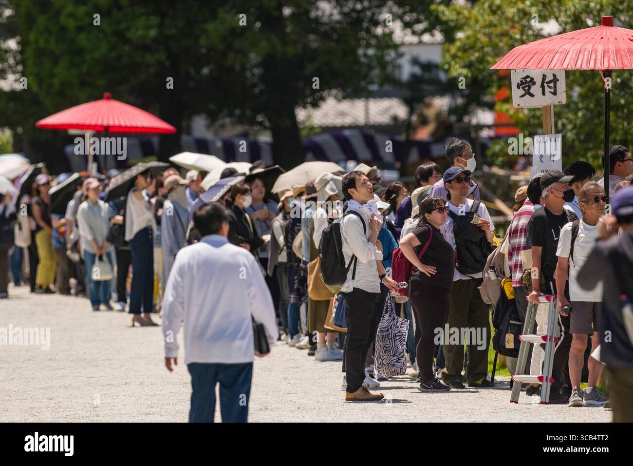 A large diverse crowd stands patiently in line under the sun before the ...