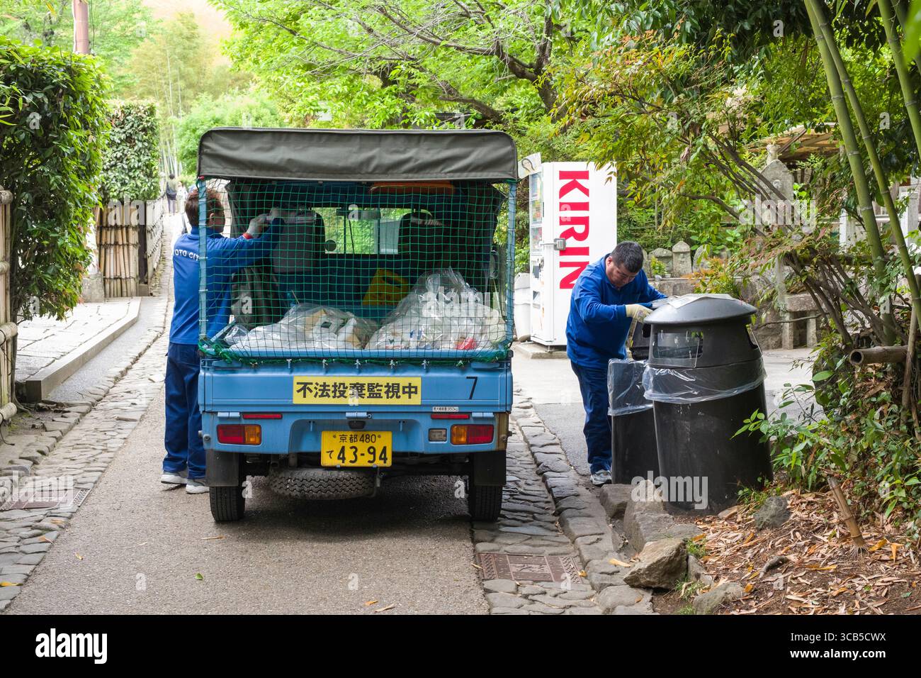 Two waste management workers are seen collecting trash in an urban ...