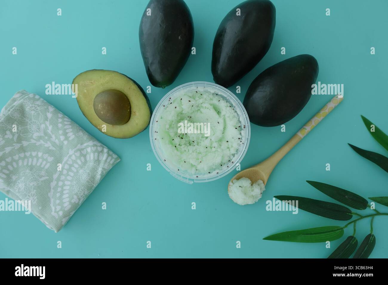 A bowl of avocado scrub surrounded by fresh avocados and a wooden spoon ...