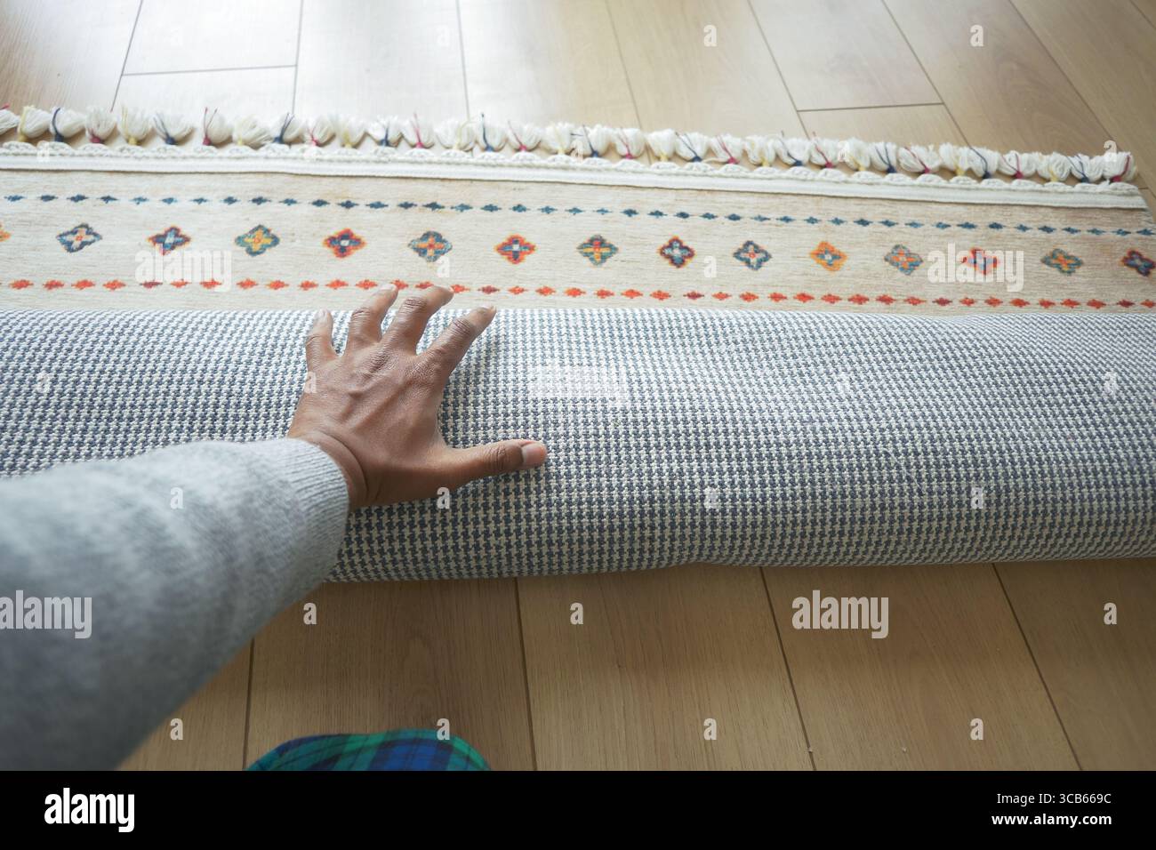 Hand rolling up patterned area rug on wooden floor Stock Photo - Alamy