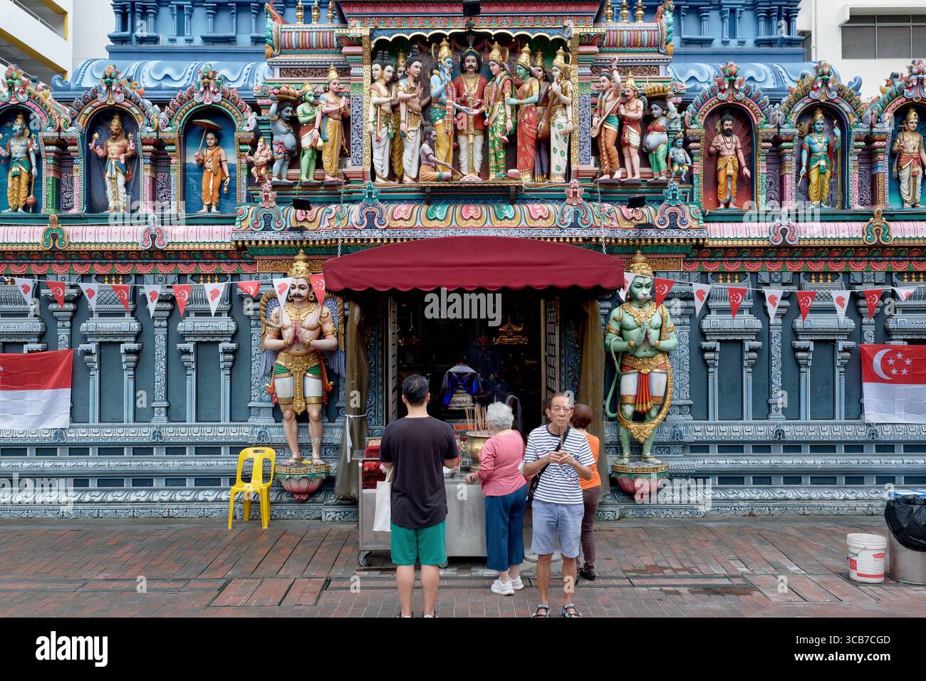 A man praying & other worshippers in front of ornately decorated Sri ...