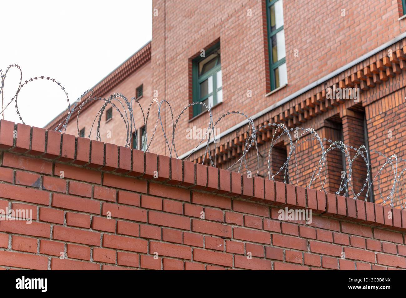 Barbed wire fence with red brick building. A coiled barbed wire fence ...