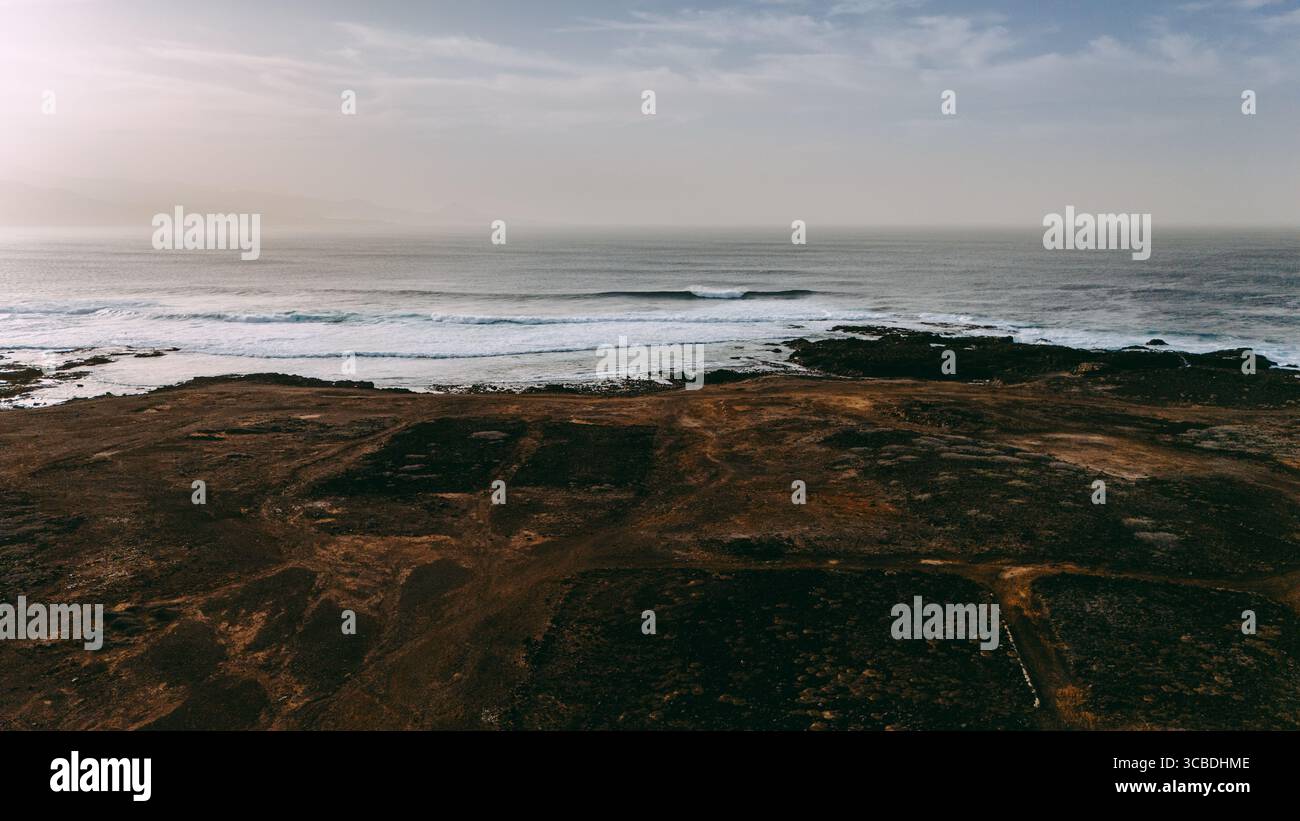 Aerial view of dark, rugged coastline where the land meets the ocean's ...