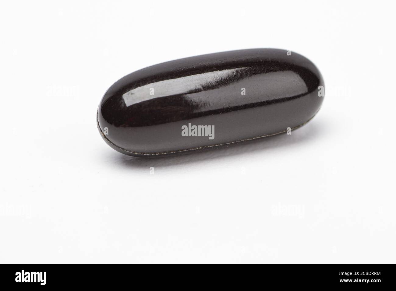 Close up view of a black omega supplement pill against a white ...