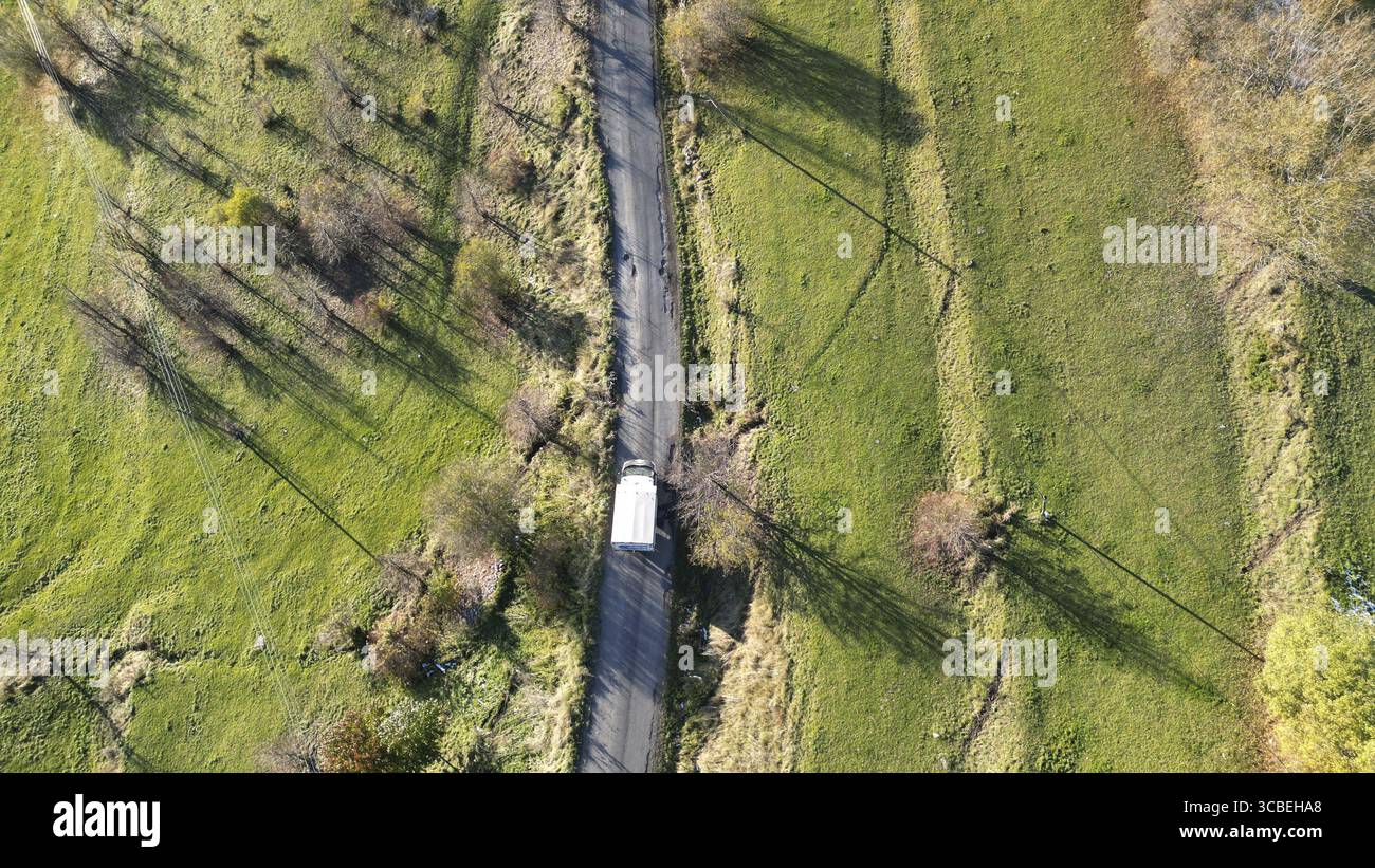 Aerial view of a lone white van navigates a narrow asphalt road cutting ...