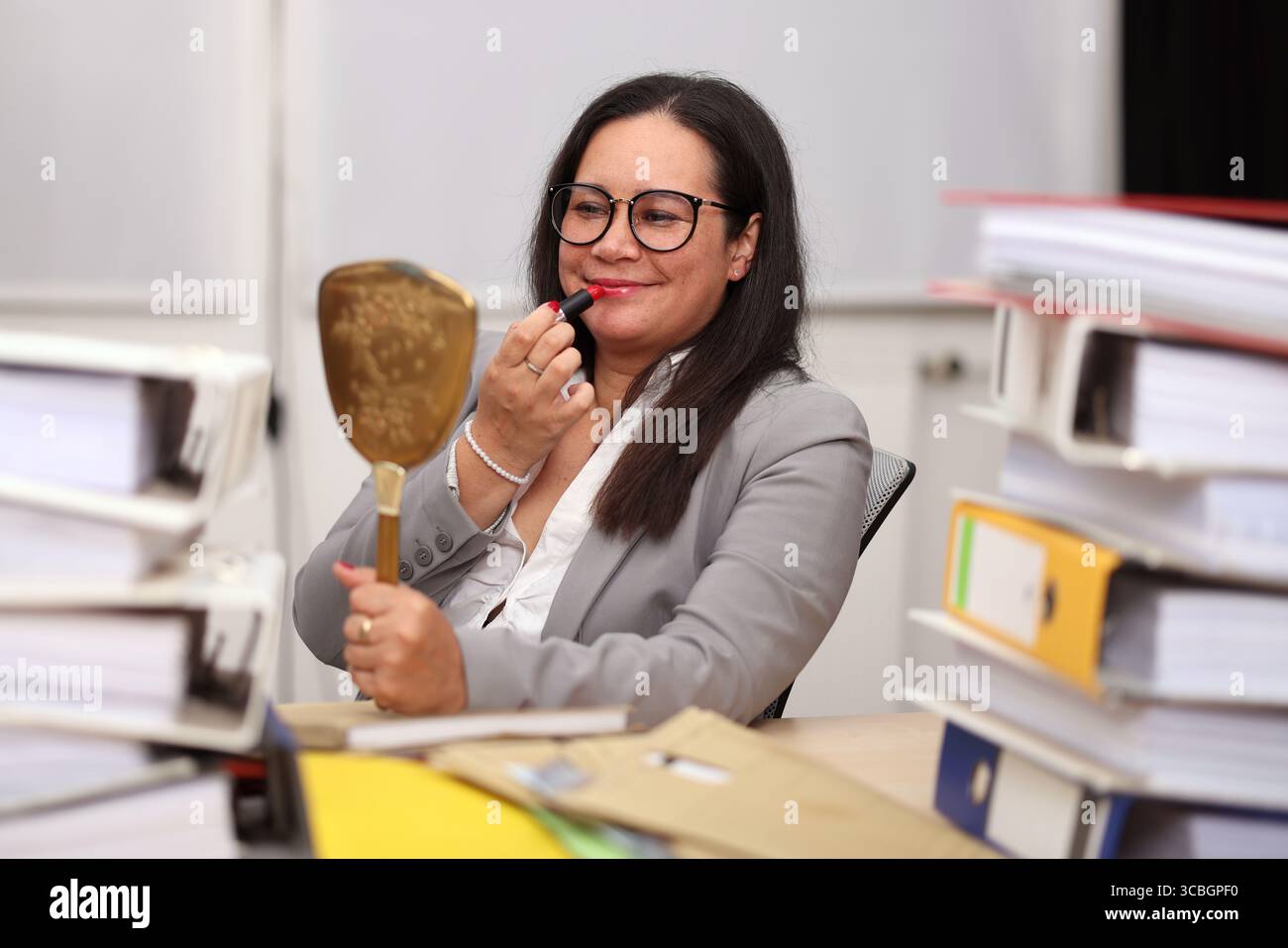 female secretary with glasses sits at the desk and applies makeup with ...