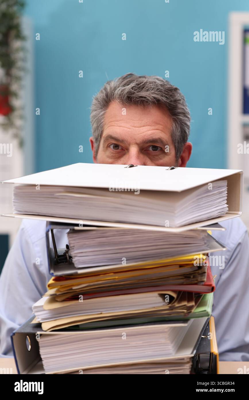 Office worker looks over a stack of files, looks concentrated Stock ...