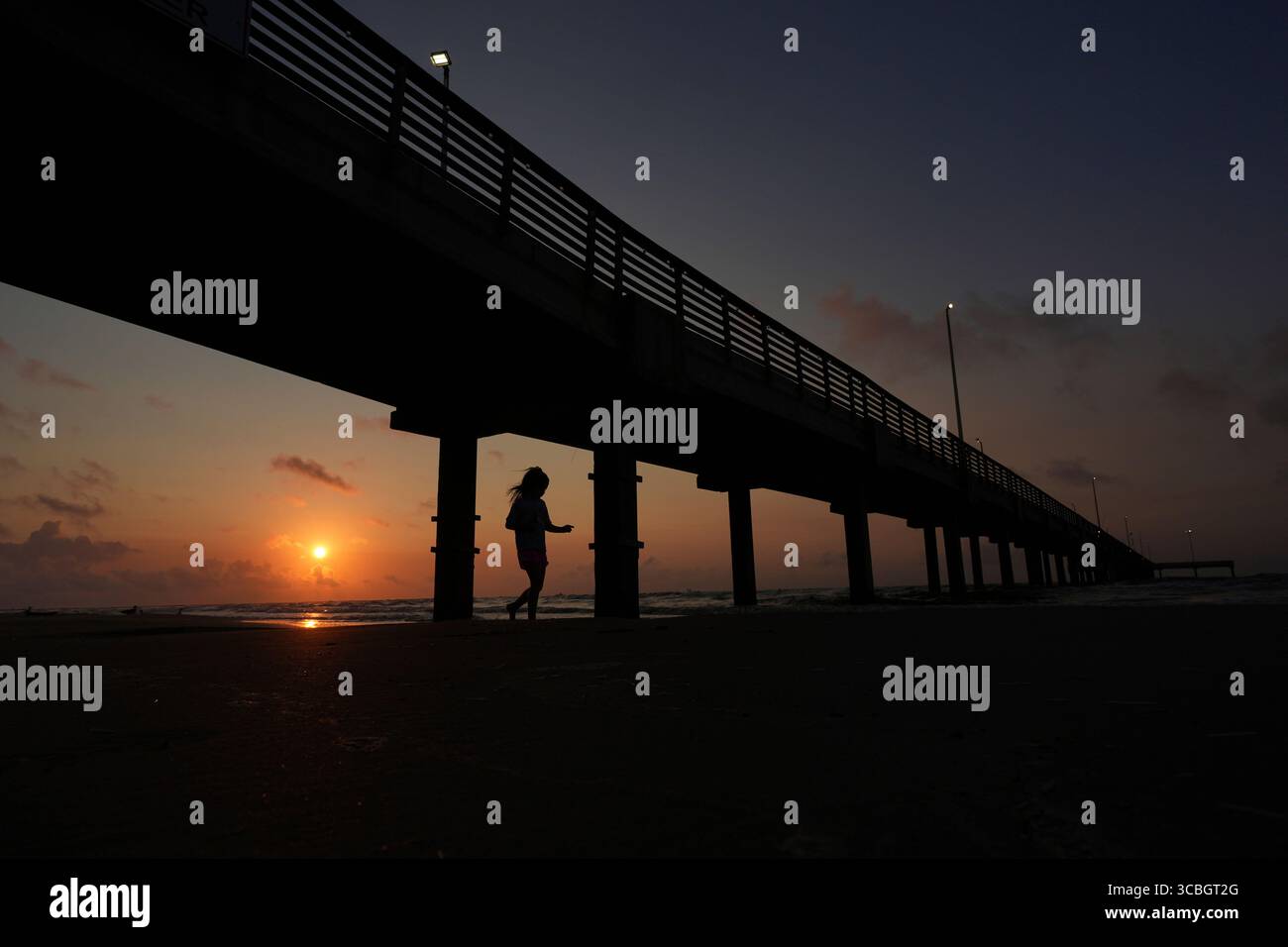 A young girl looks for sea shells as the sun rises in Port Aransas ...