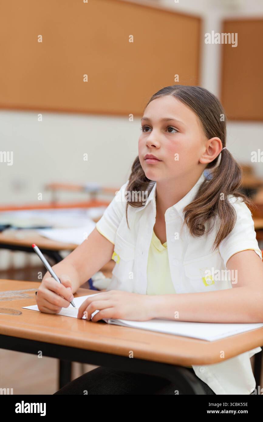 Girl student sitting at wooden desk in classroom with bulletin boards ...
