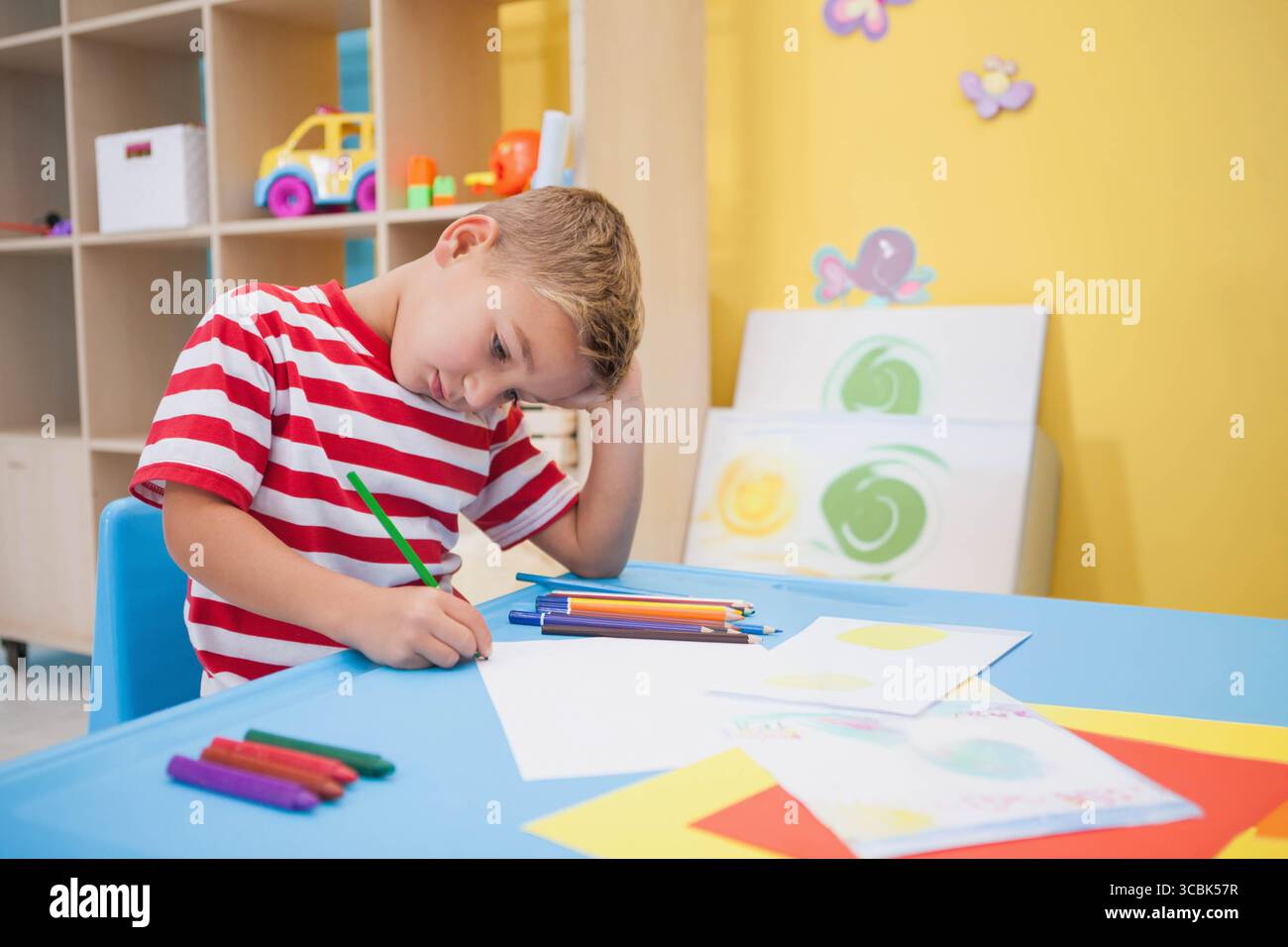 Boy drawing with colored pencils at blue table in children's activity ...