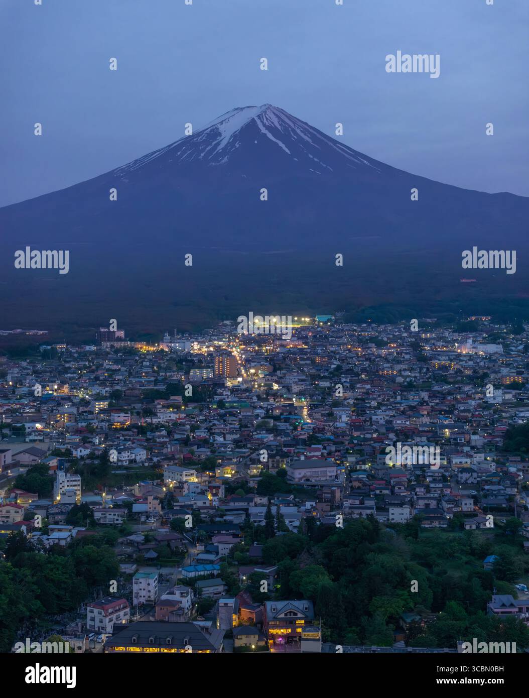 Aerial view of Mount Fuji looming majestically over a town, lights ...