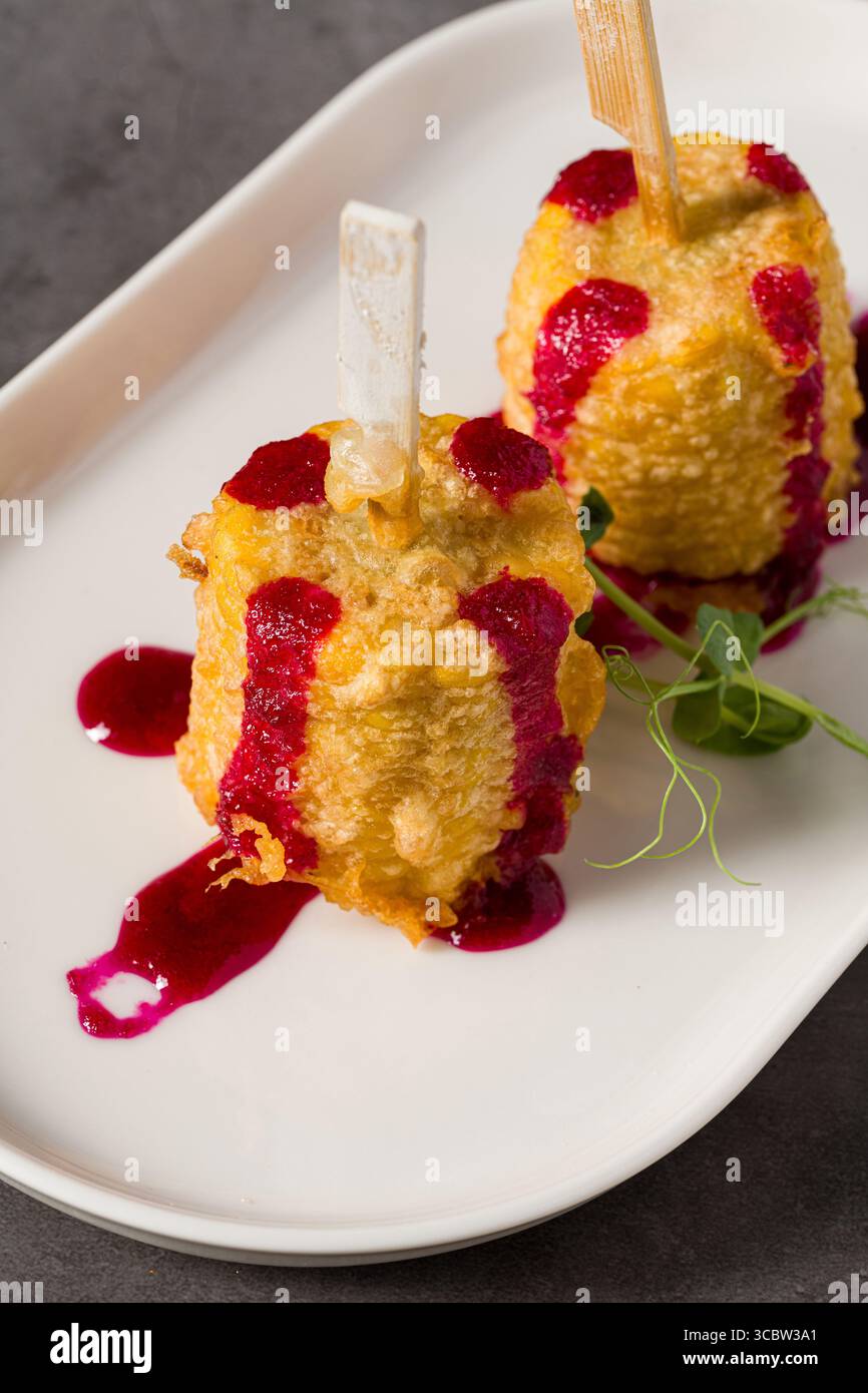 Deep-fried corn tempura on sticks with beetroot puree and microgreens ...