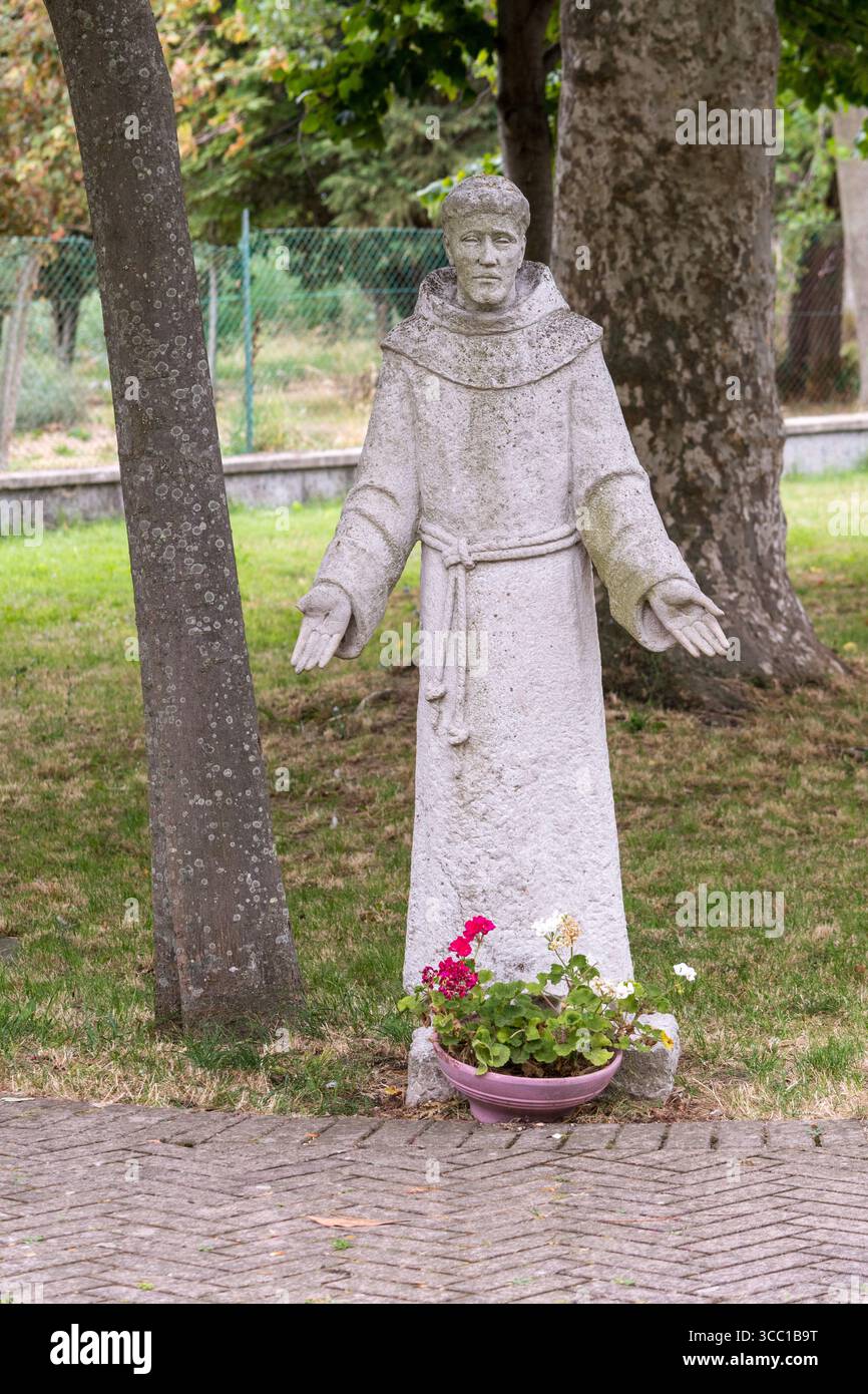 Stone statue of a friar with open arms, standing among trees in Barbana ...