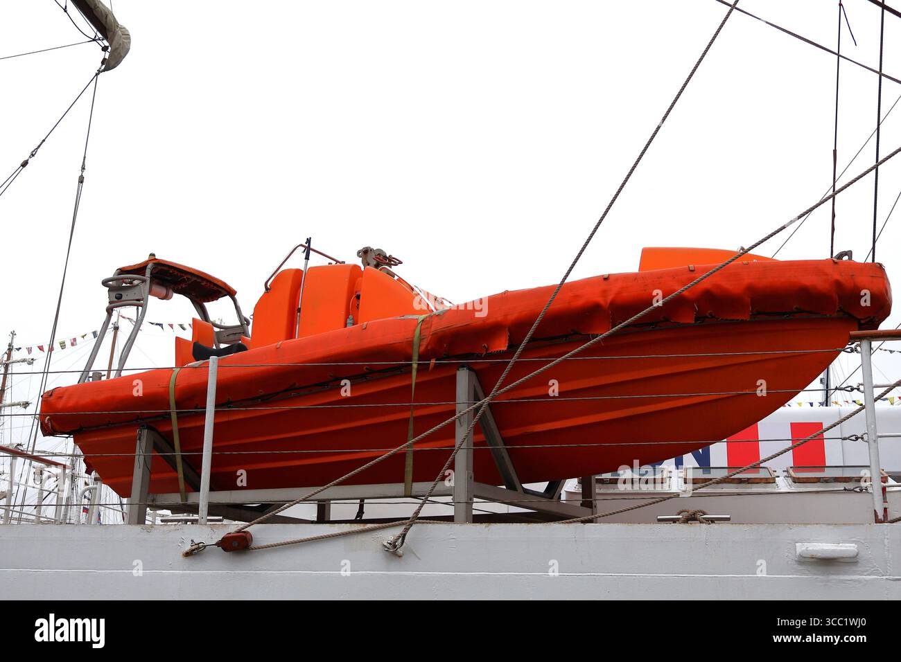 An orange lifeboat hanging on the side of a tall ship Stock Photo - Alamy