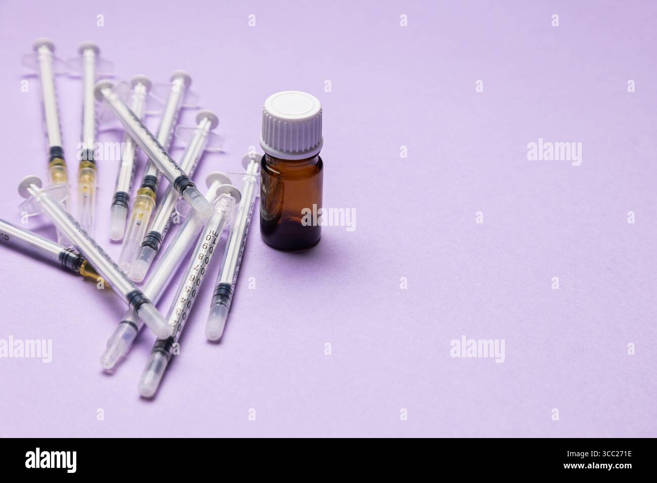 Medical syringes with needles scattered around a small amber glass vial ...