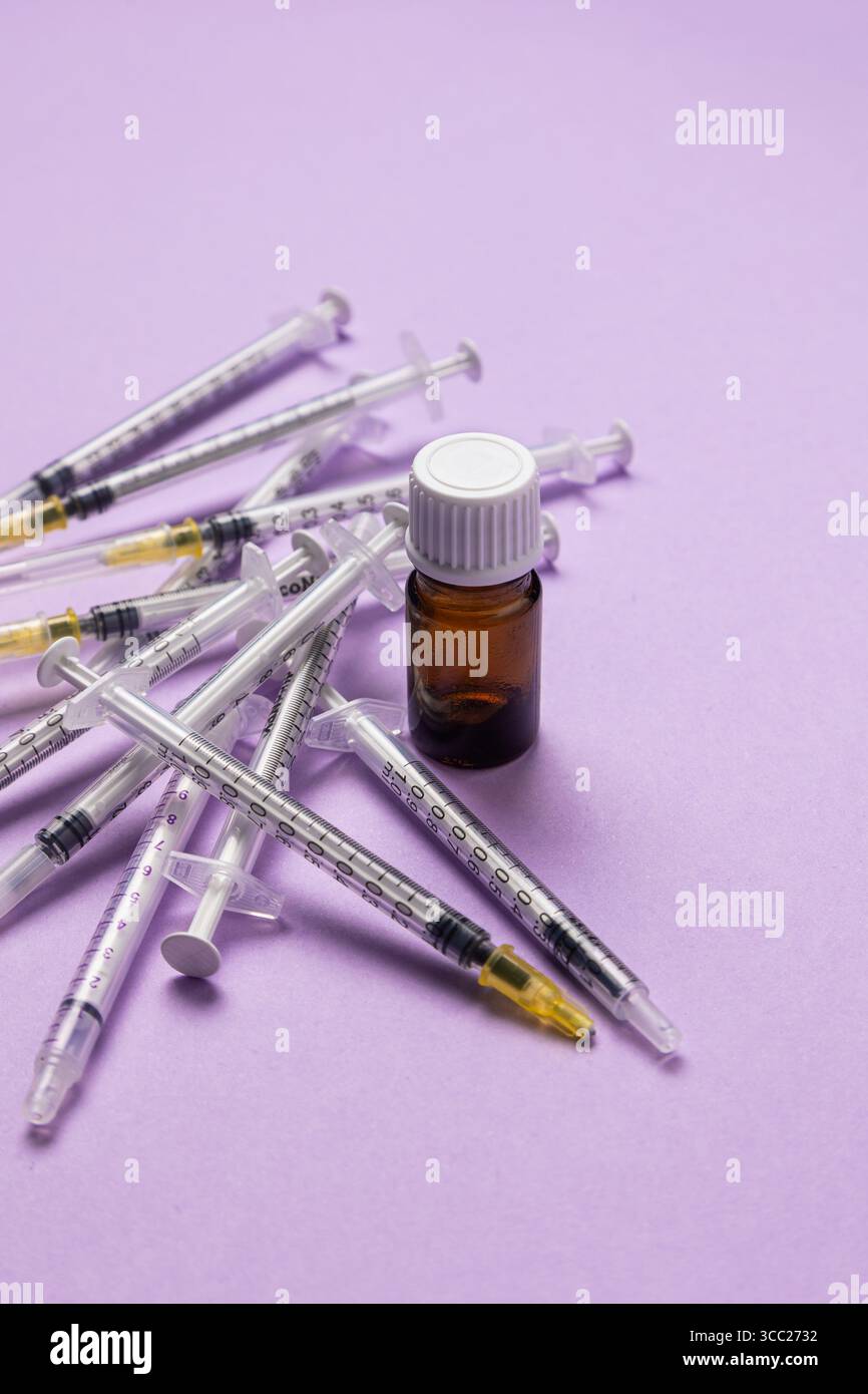 Medical syringes with needles scattered around a small amber glass vial ...