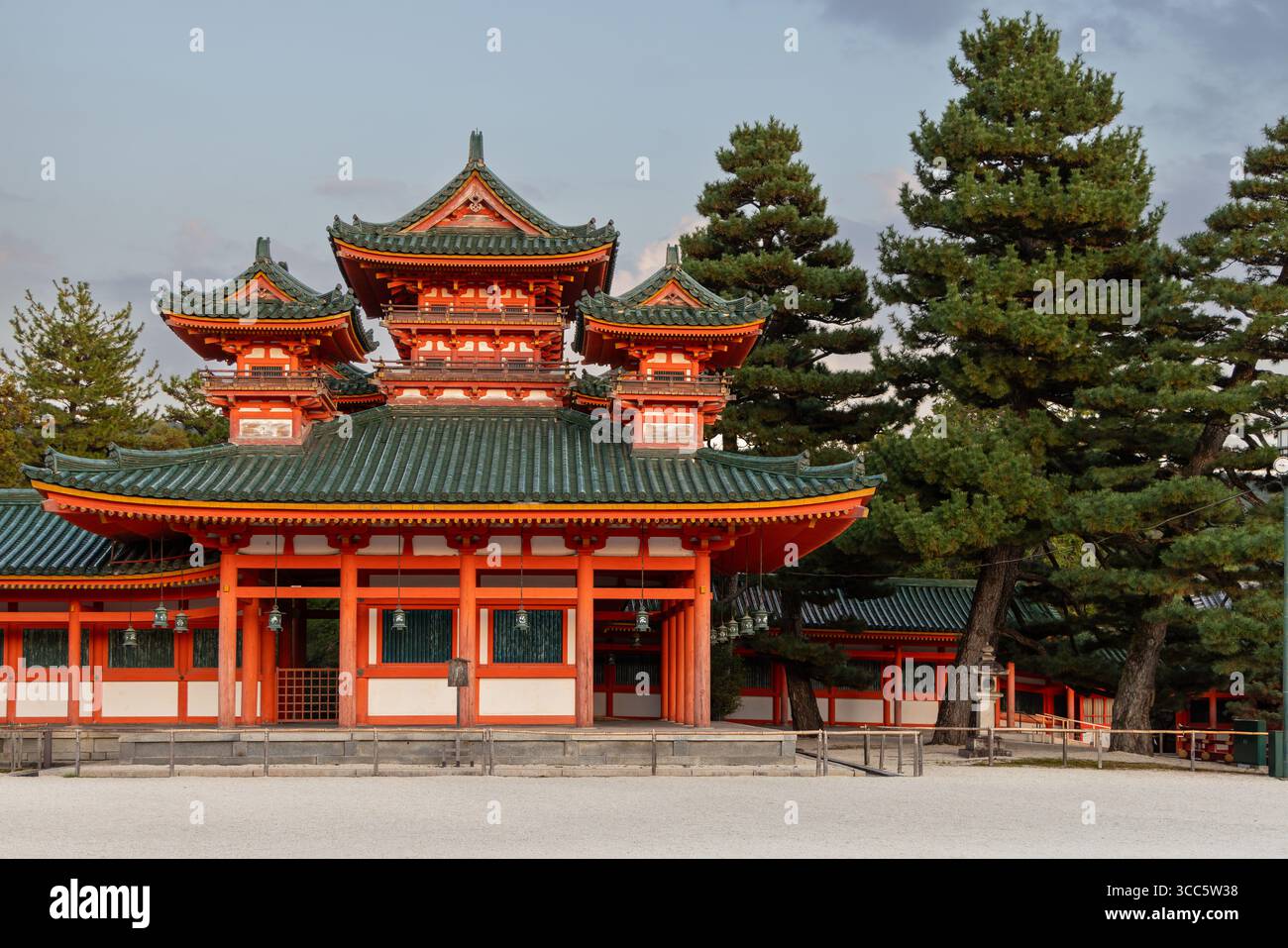 Framed by ancient pines, vivid facade of Heian Jingu Shrine in Kyoto glows in soft light ...
