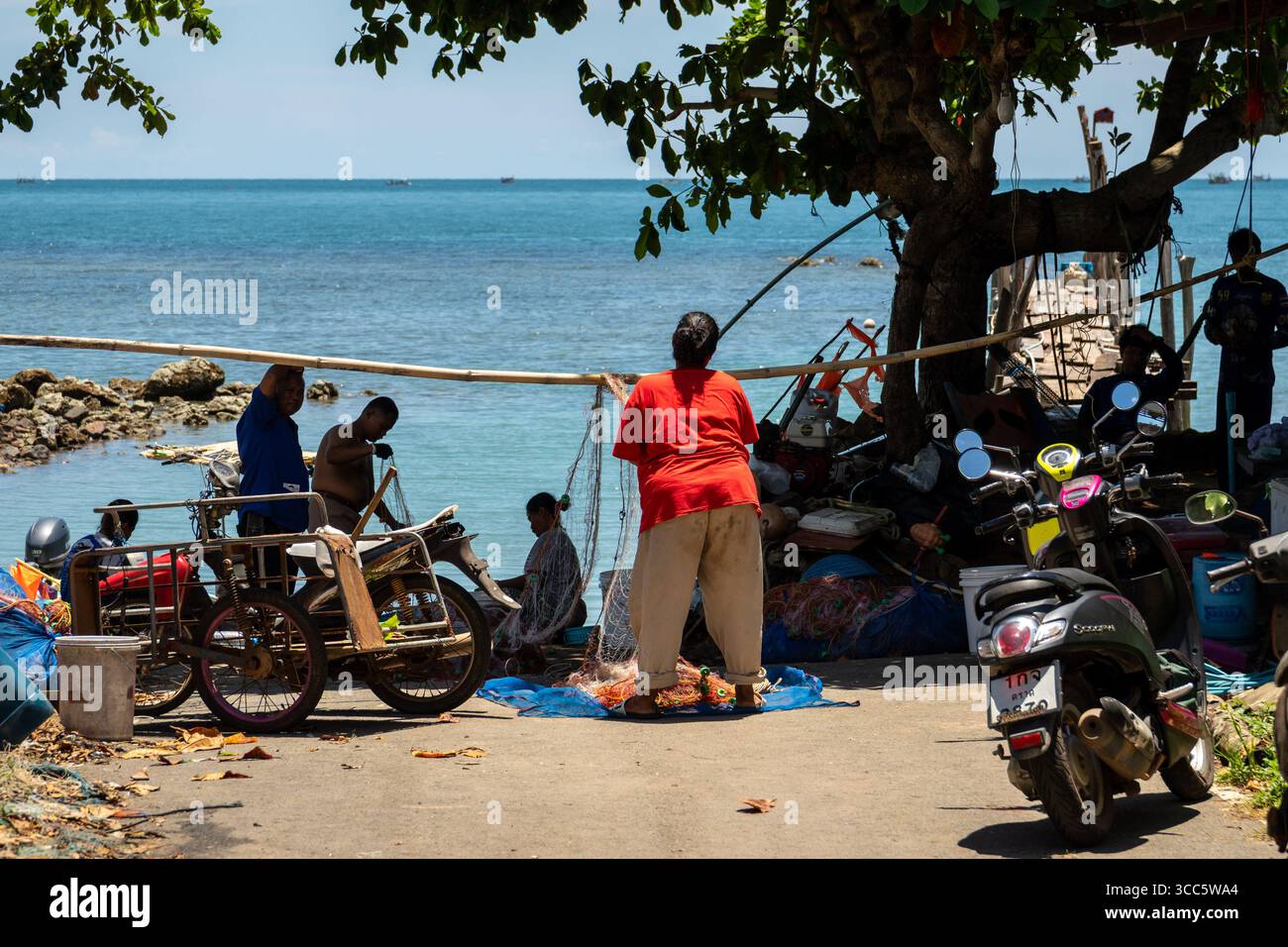A woman (in red) untangling a fishing net, surrounded by other members ...