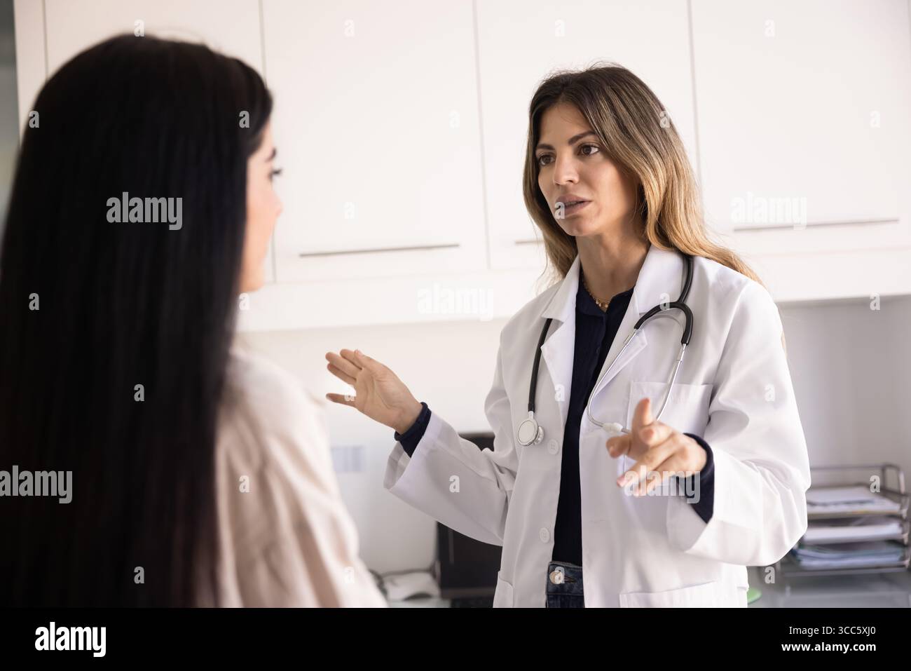 Serious doctor woman in lab coat talking to female patient Stock Photo ...
