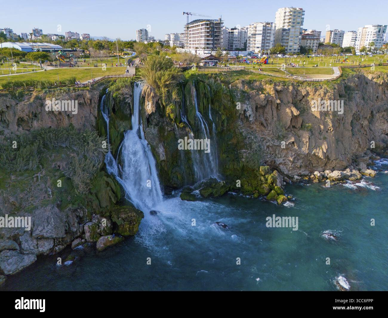 A waterfall cascades from a cliff into the sea, surrounded by urban ...