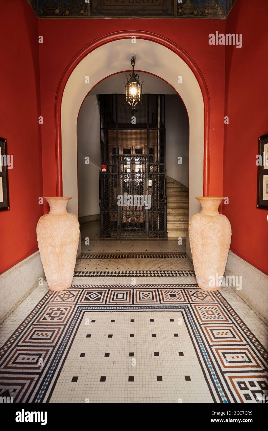 Elegant hallway in Rome with red walls, mosaic floor, and antique vases ...