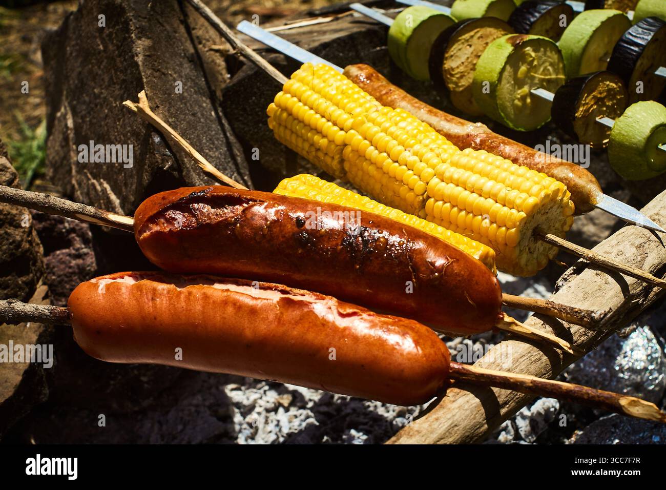 Outdoor picnic: sausages, corn, and vegetables on skewers, cooking over ...