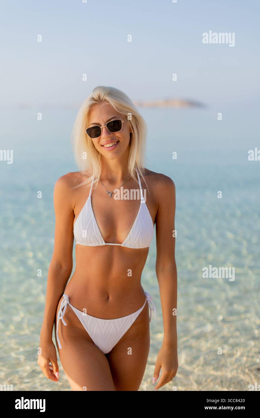 A model poses at the beach, adorned in a striking white bikini, radiating joy while basking in ...