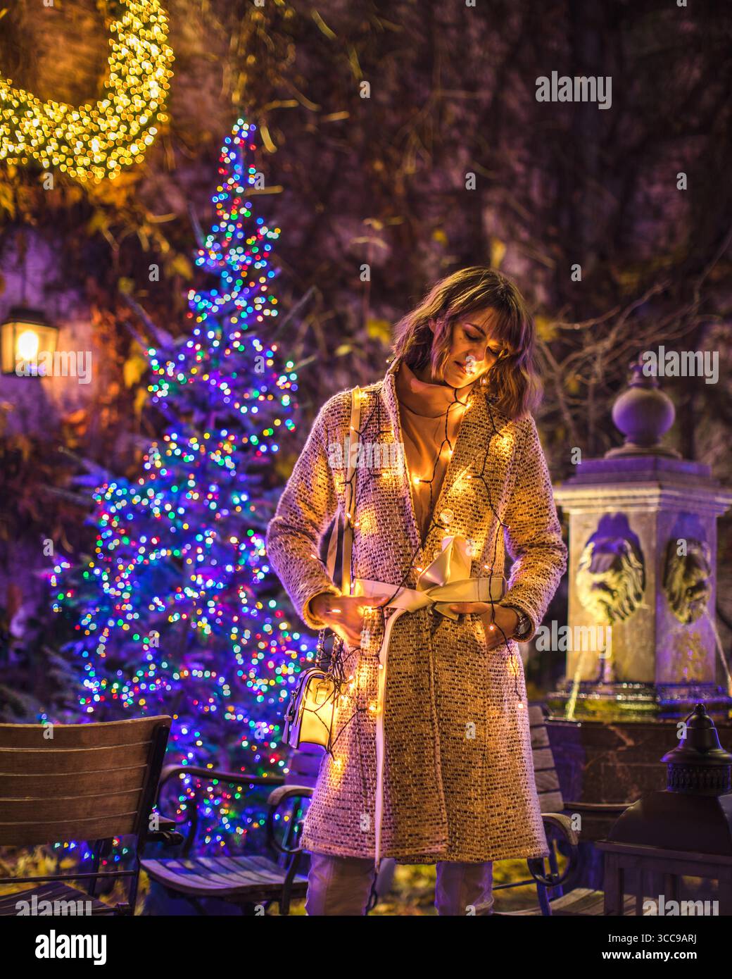 Beautiful young woman in winter outfit having fairy lights around the ...