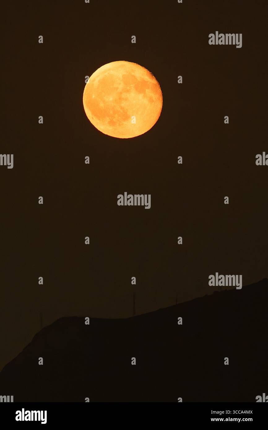 Orange full moon glowing in the dark sky, illuminating the mountain ...