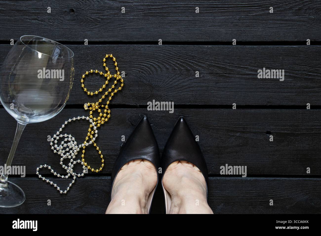 Female legs in black high heels, empty wine glass and beads lying next ...