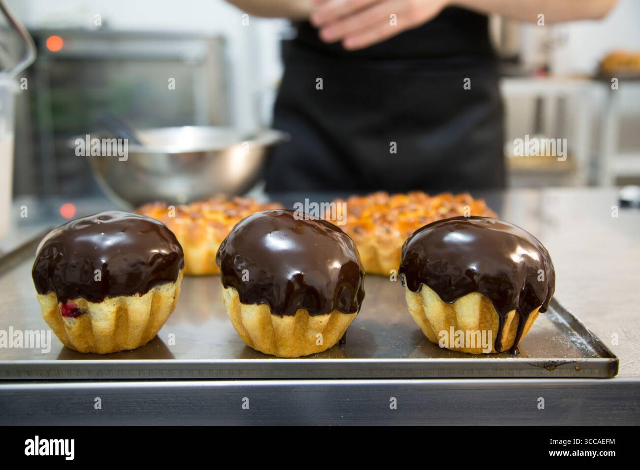 Chocolate glazed rum baba cakes on tray with chef’s hands in frame ...